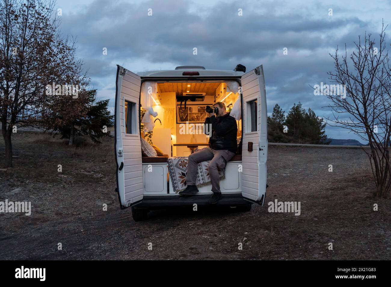 Mature man taking photos from the back of his camper van during sunset ...