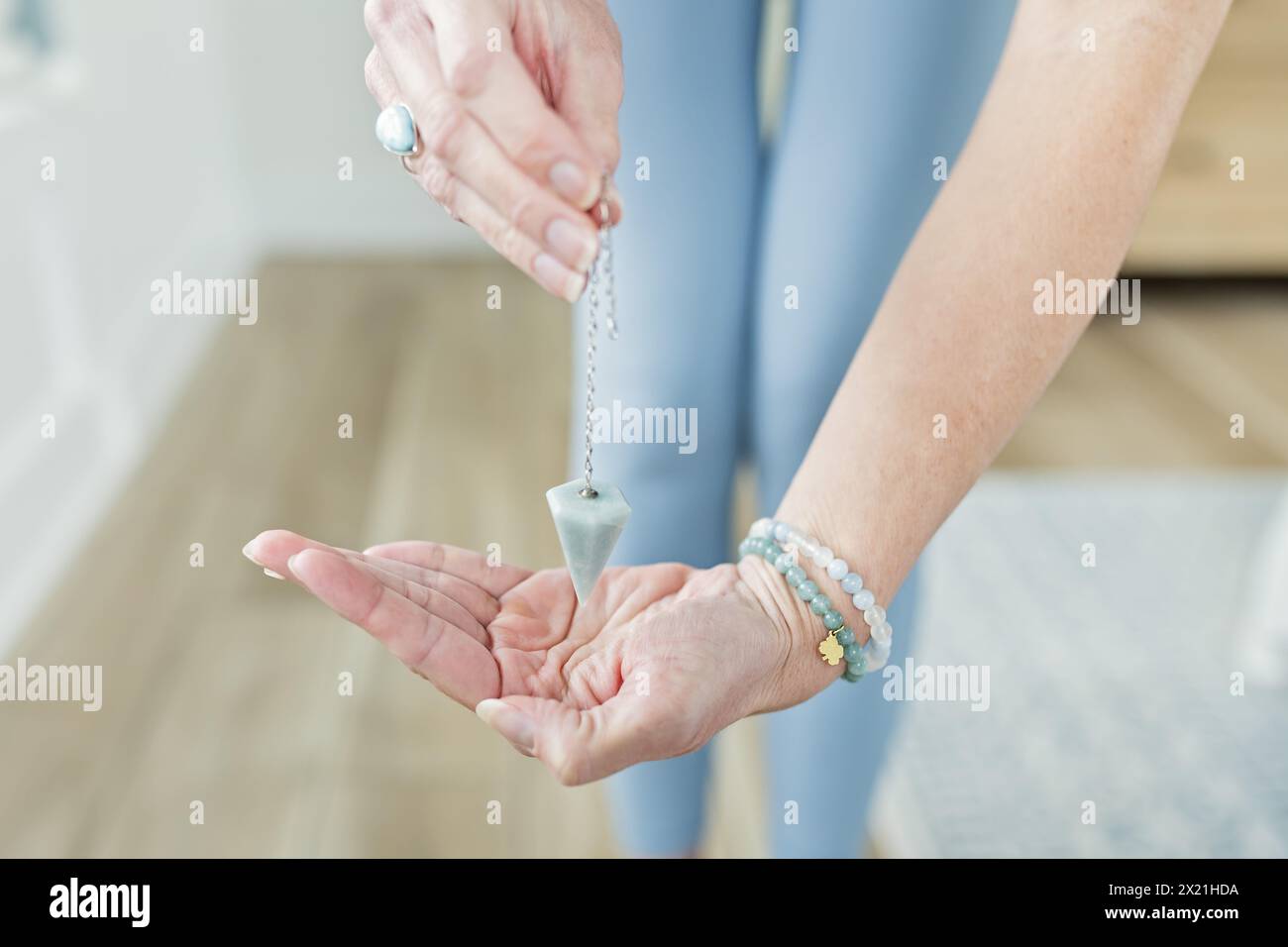 Woman holding pendulum over hand wearing crystal bracelets and ring ...