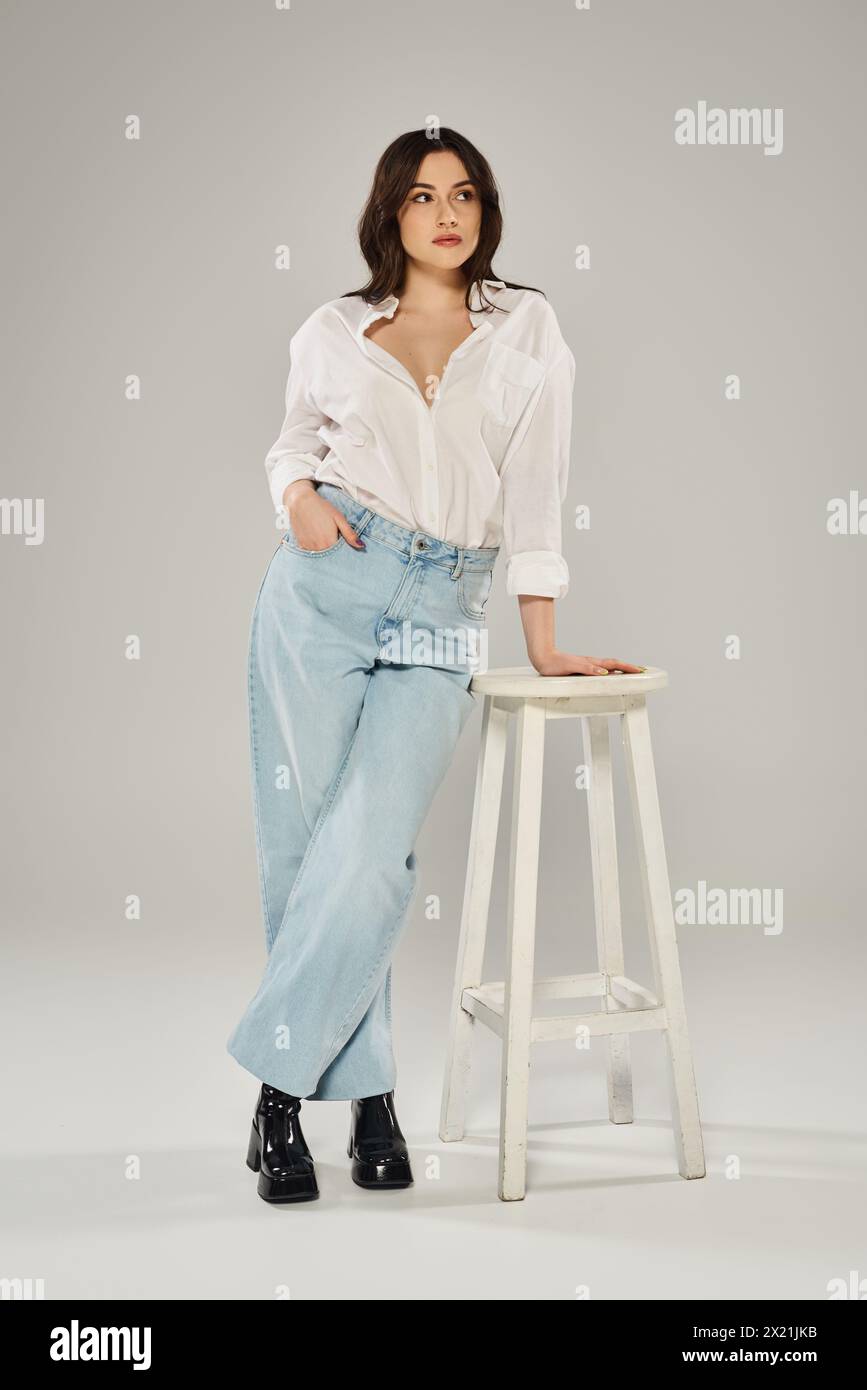 A beautiful plus size woman in a white shirt and jeans poses gracefully ...