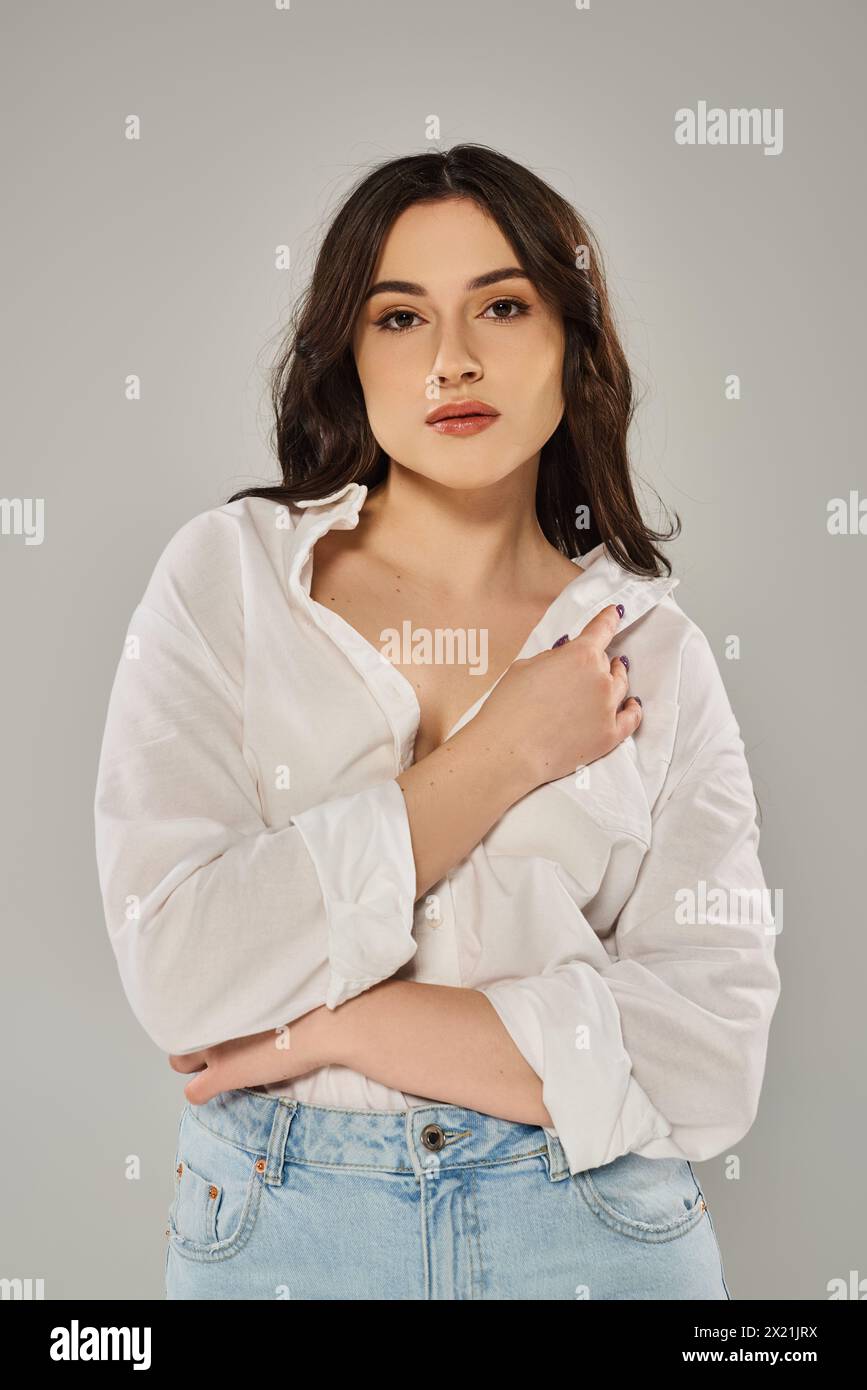 Stylish plus-size woman posing in trendy white shirt and jeans against ...