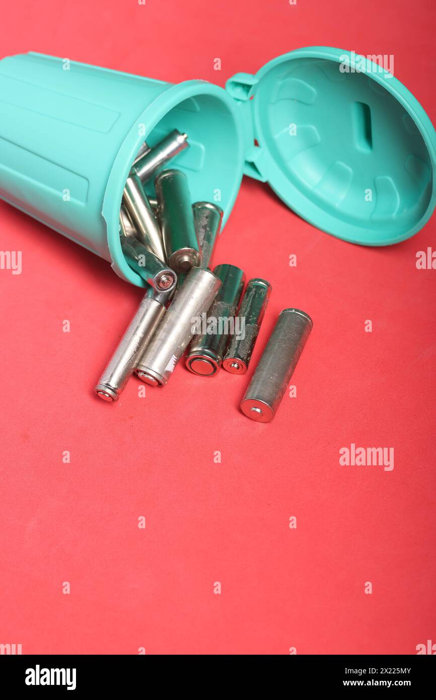 Used finger batteries in a miniature trash can. Pink background. Field ...