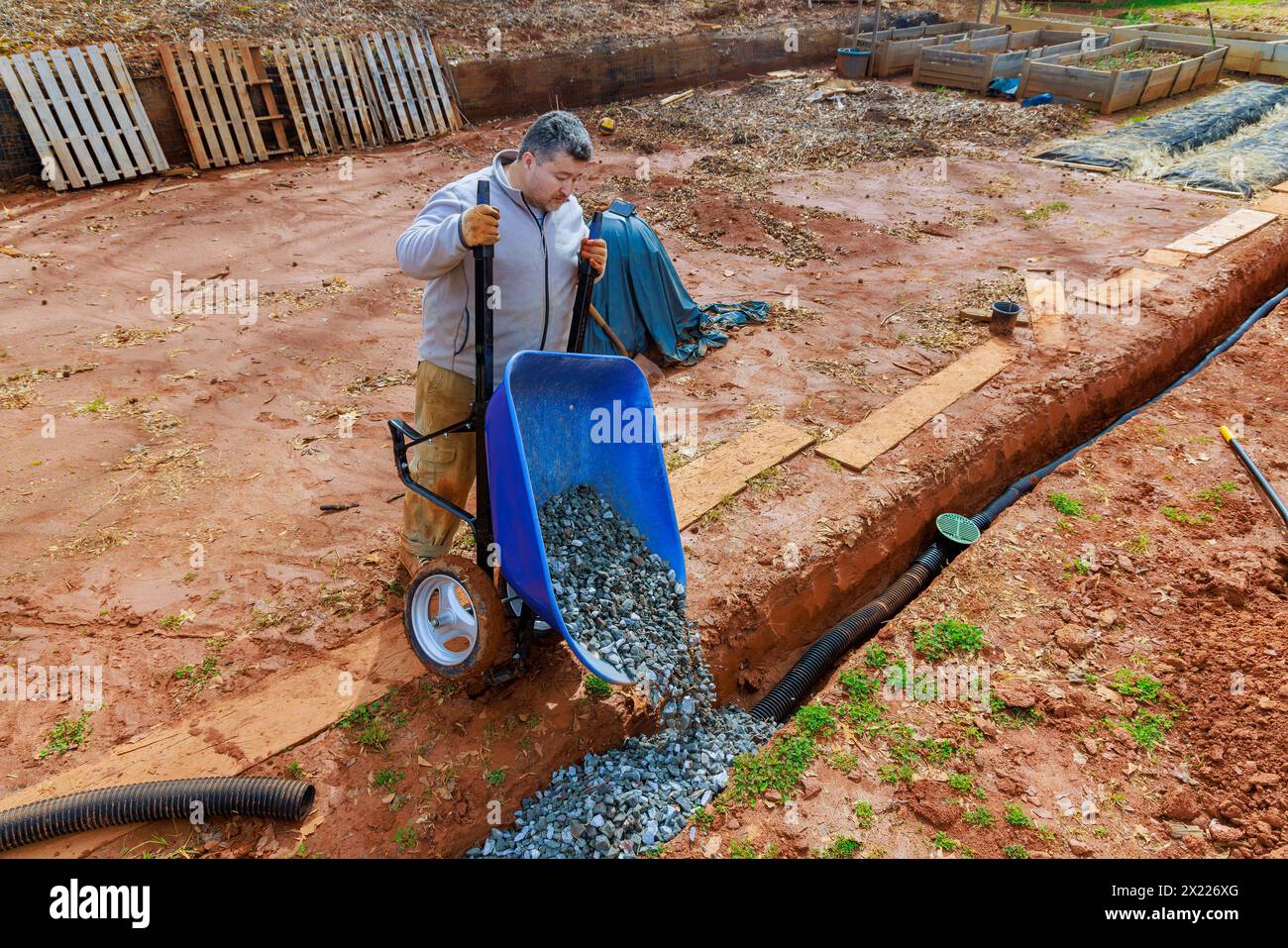 Worker fills drainage pipe with crushed stone from wheelbarrow Stock ...