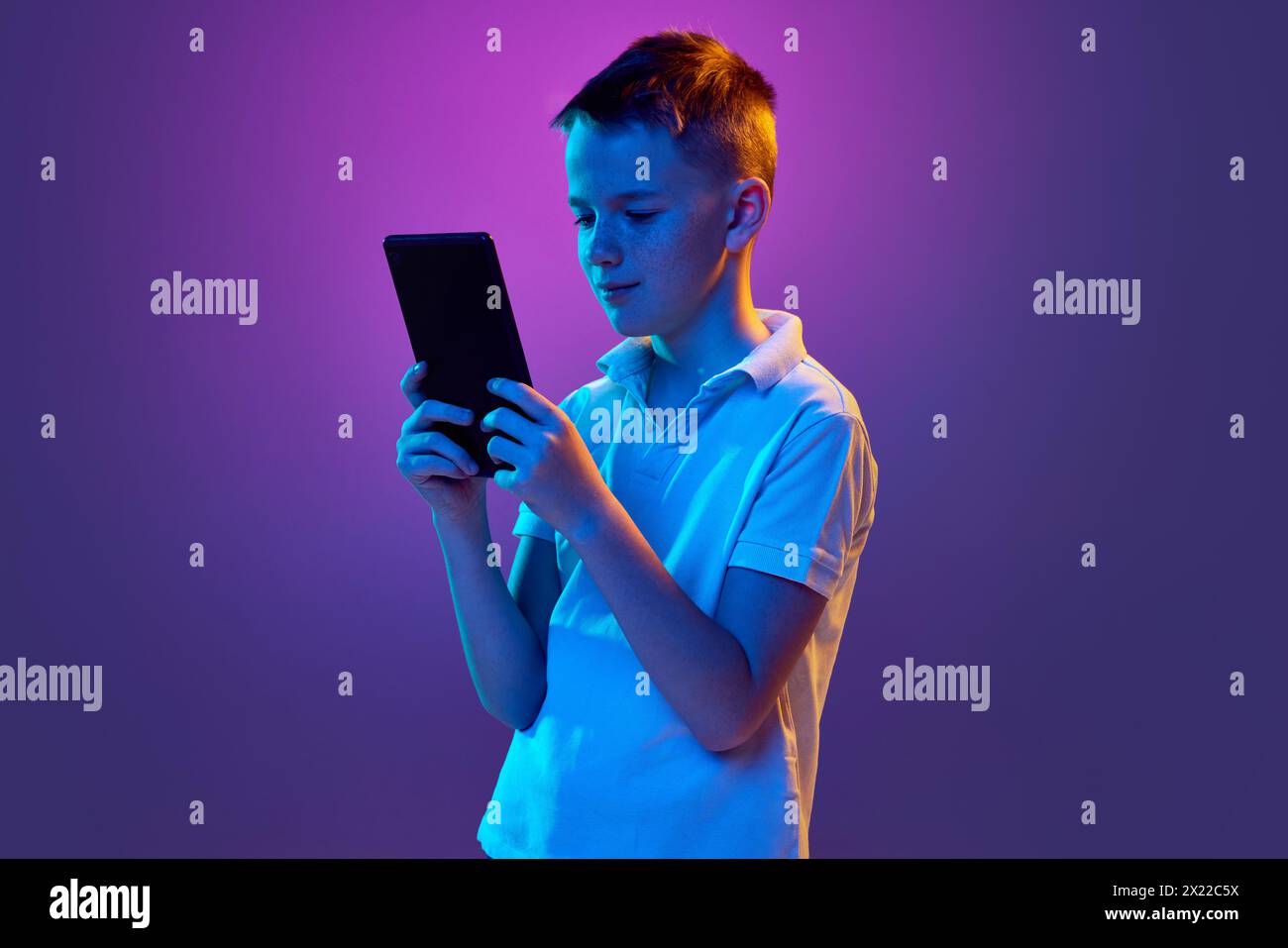Cute boy, teenager looking at tablet screen in neon light against ...