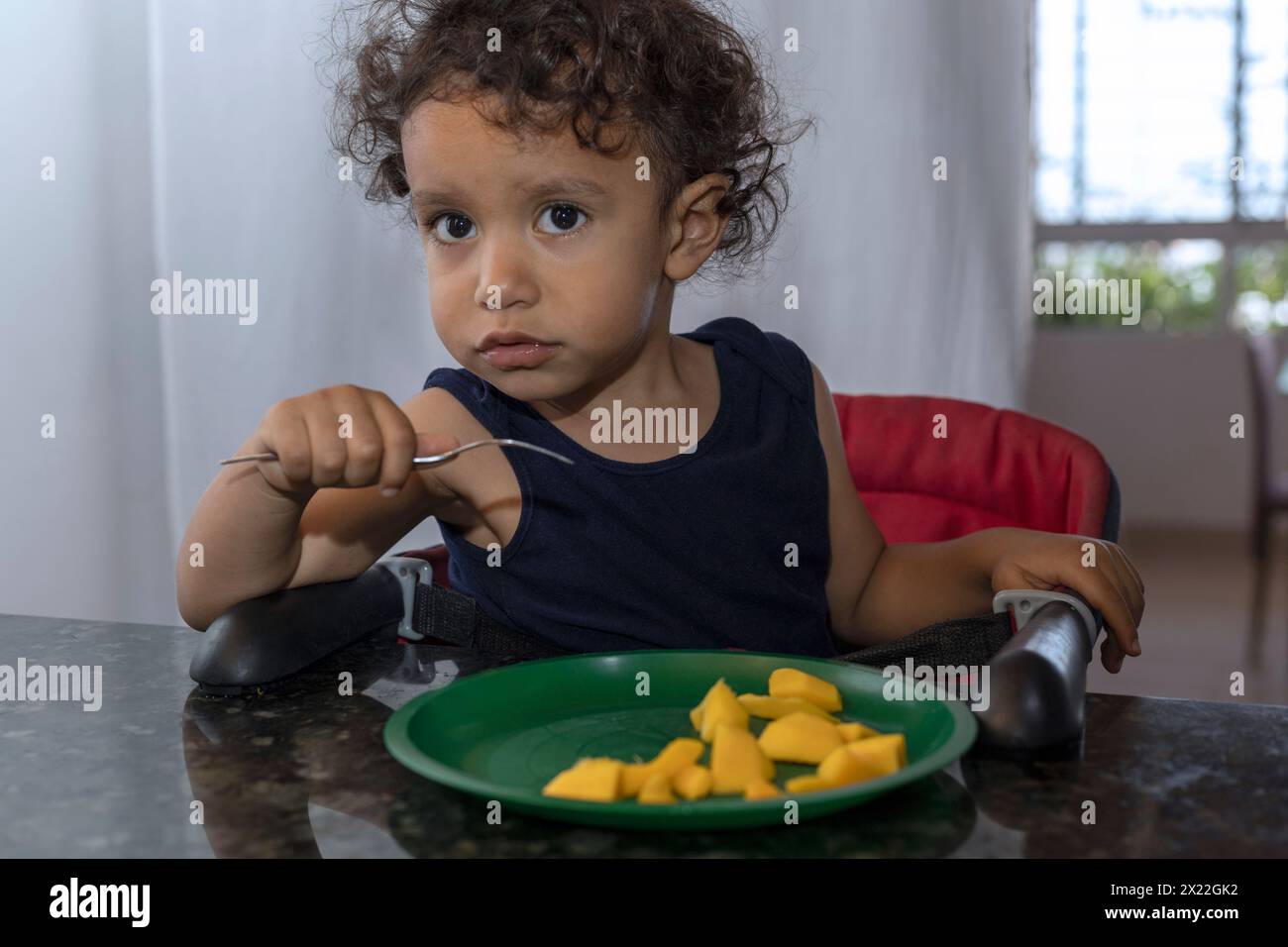 Latin American boy sitting in his chair eating his fruits alone, he is ...