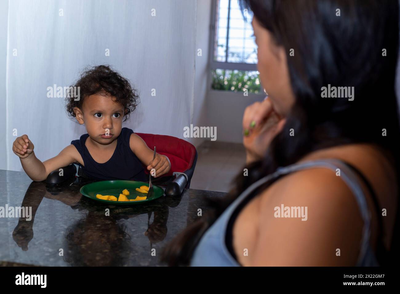 Latin American boy sitting in his chair eating his fruits alone, he is ...