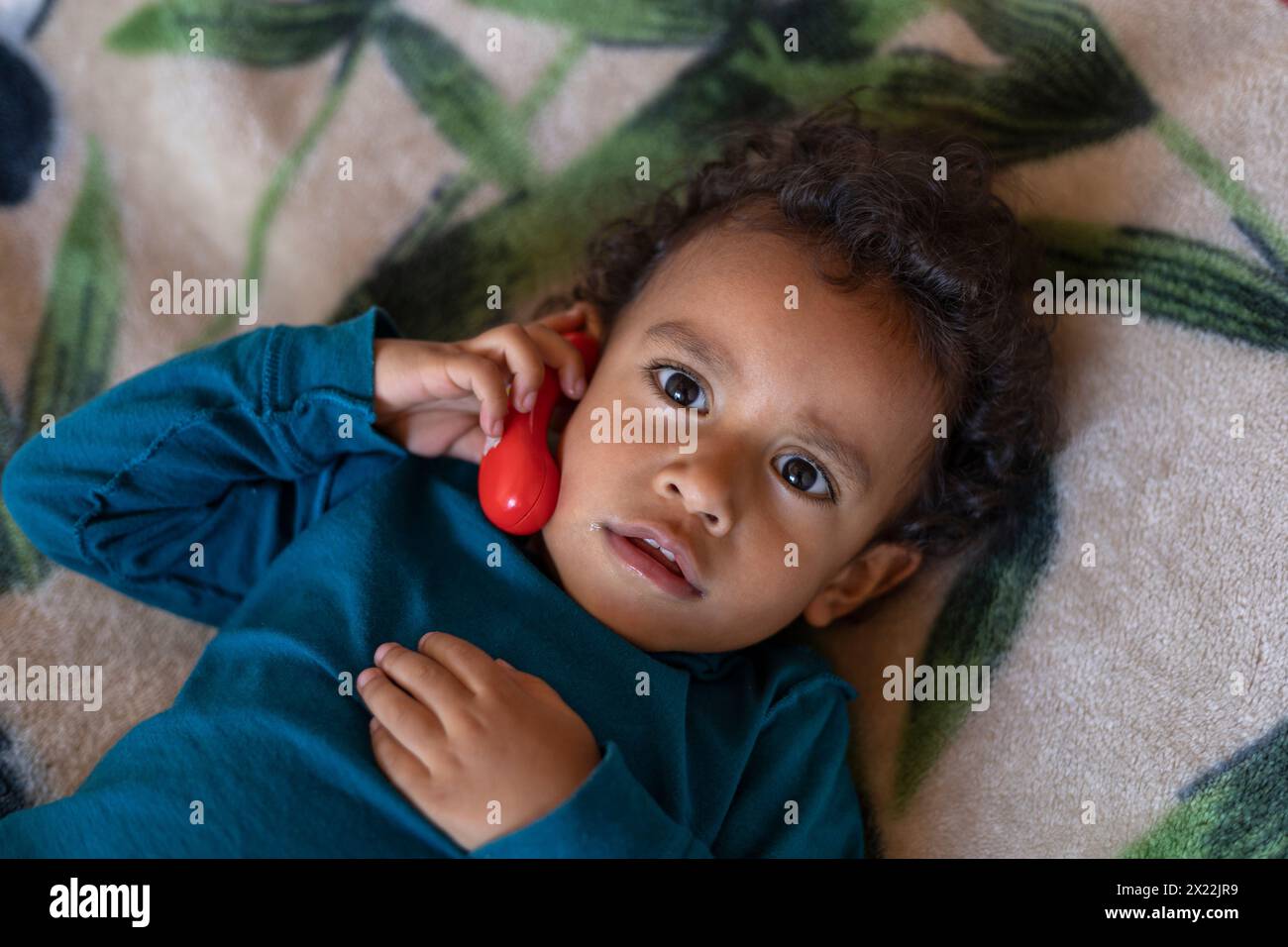 Latin American boy (2) holds a toy headset to his ear while playing on ...