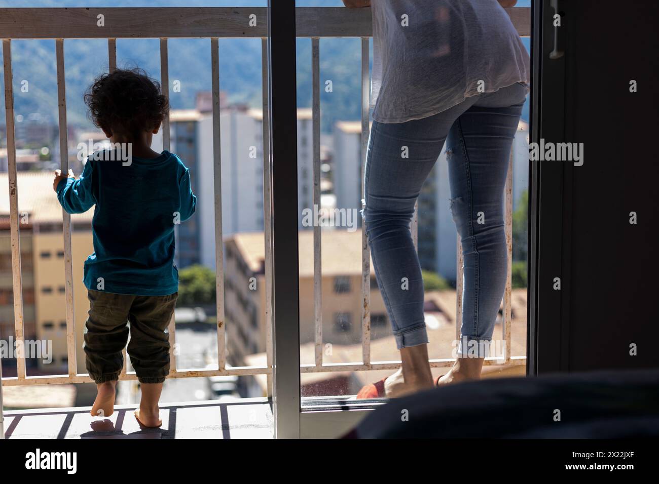 Latin American mom (30) and her son (2), standing on the balcony look ...