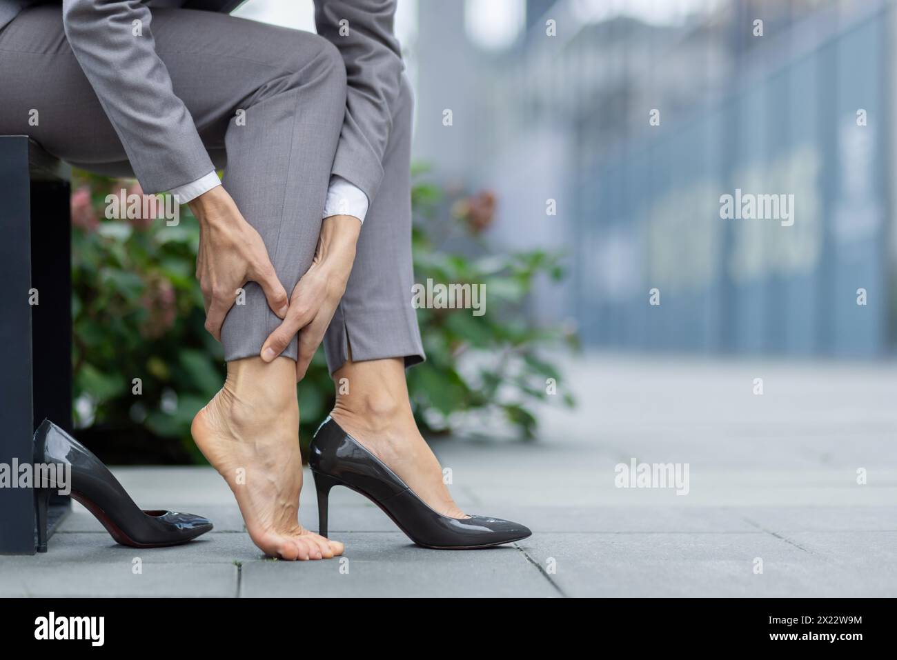 A businesswoman in a tailored suit is seated on a bench, removing her ...