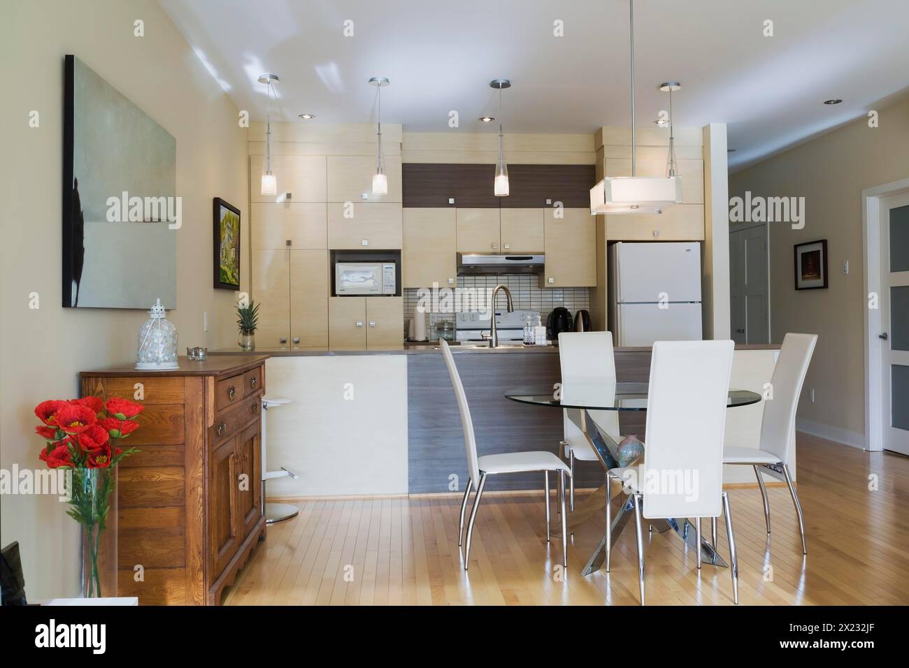 Dining room with round glass table, white leather high -back chairs and kitchen inside a ...