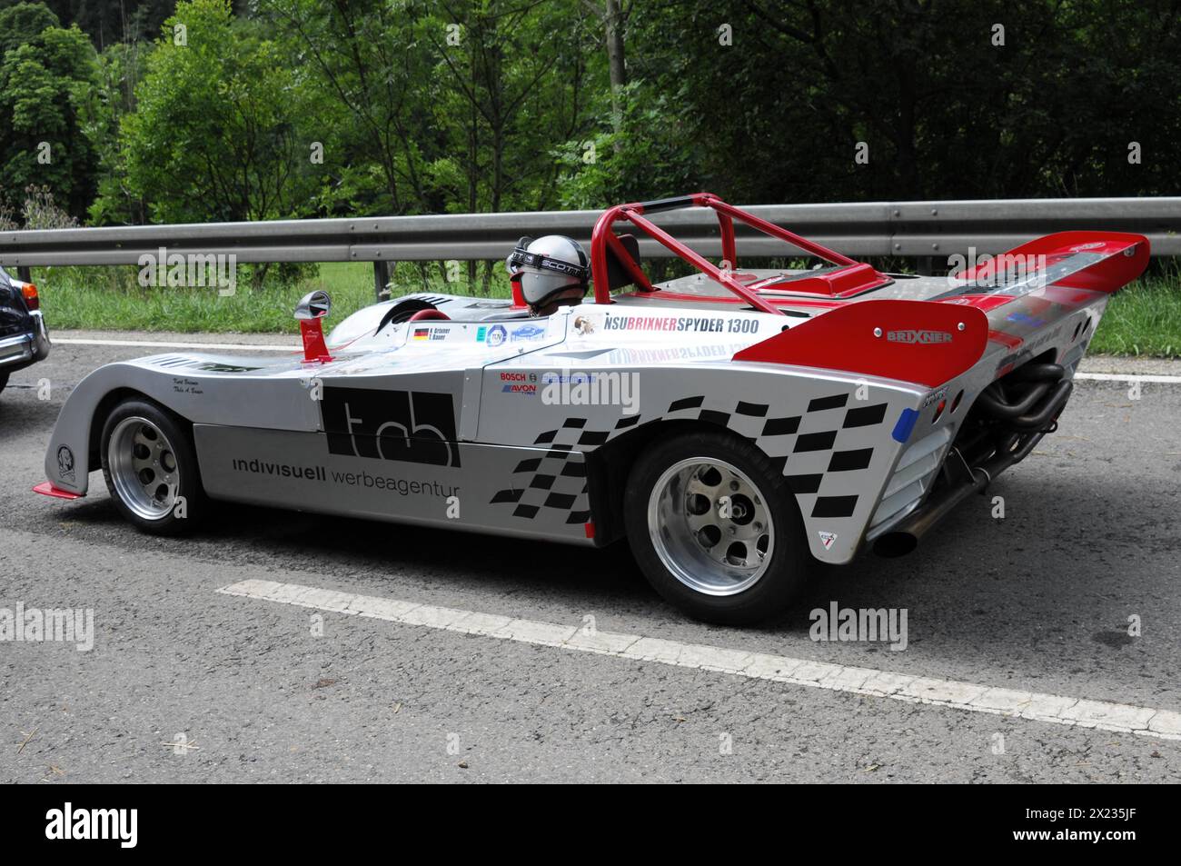 A white and red racing car with sponsor logos drives along a country ...