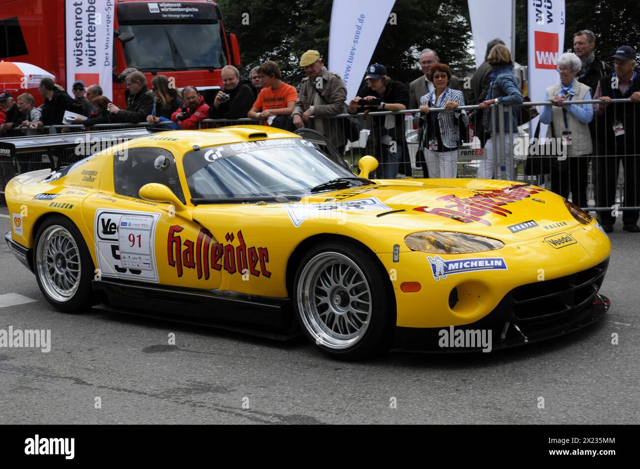 A yellow racing car full of advertising drives past spectators on a ...