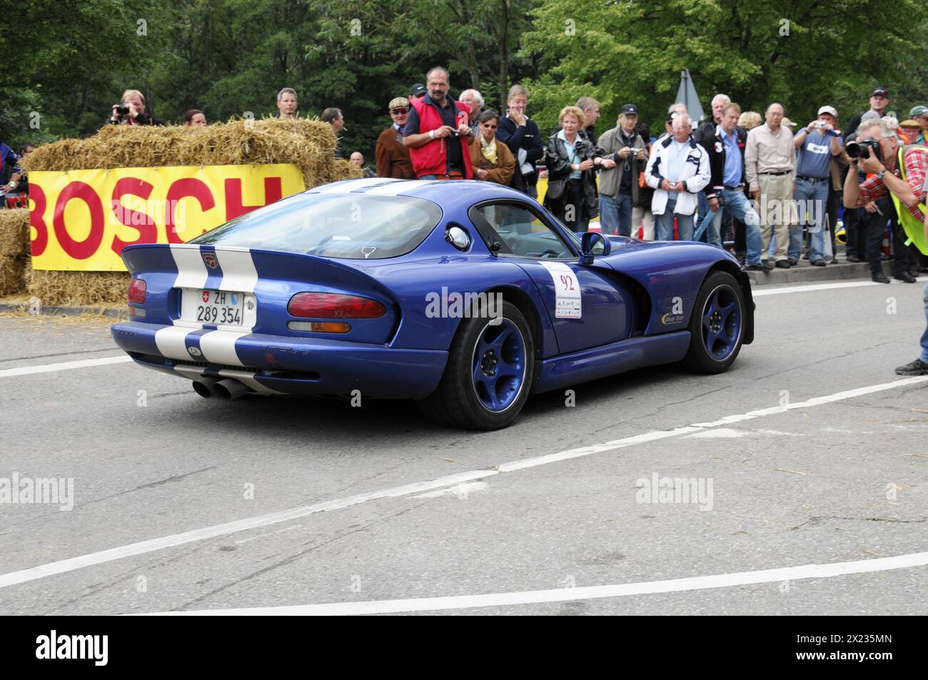 A blue sports car with a racing number and white stripes drives along a ...