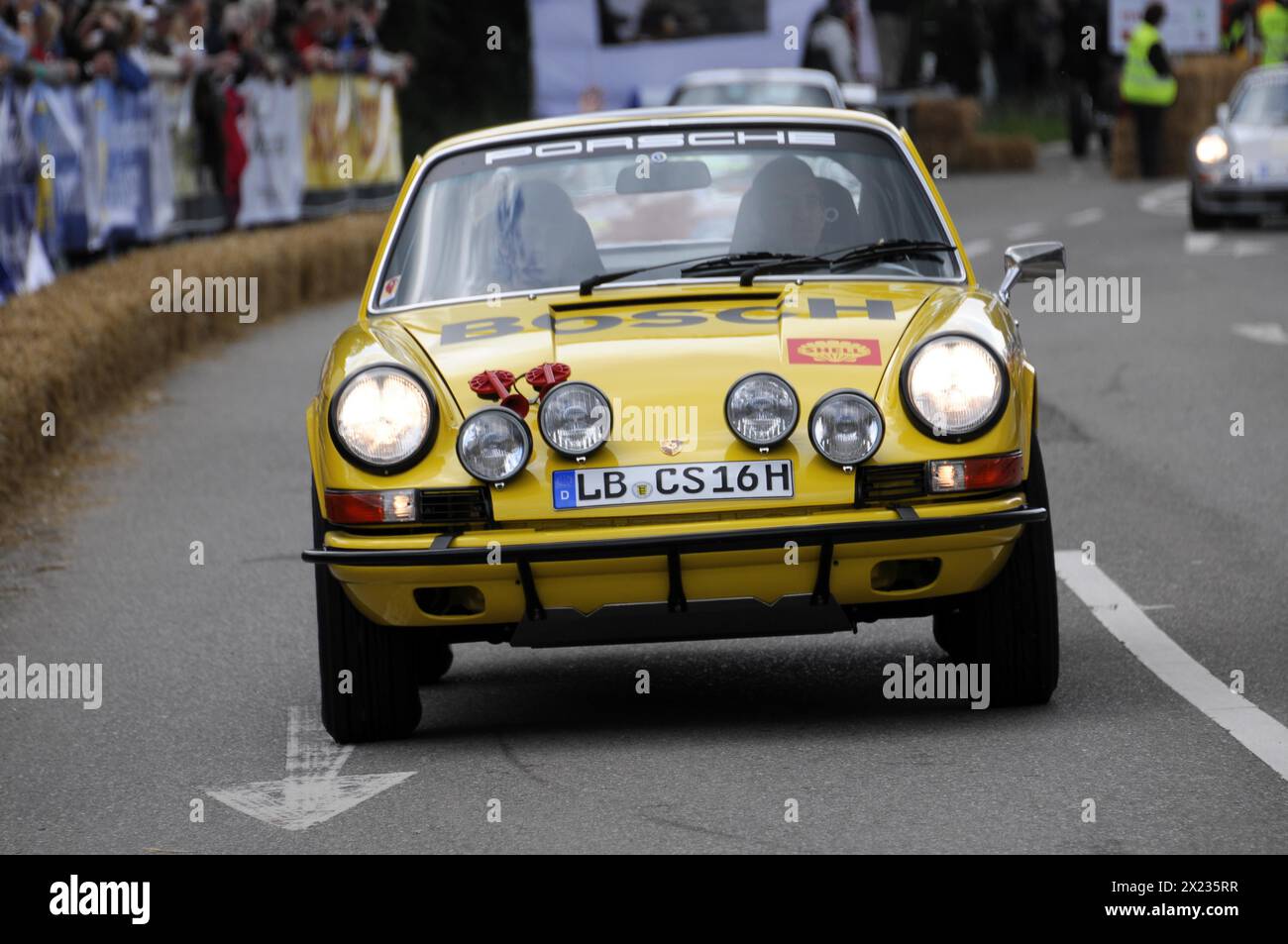A classic yellow Porsche 911 on a rally track, flanked by spectators ...