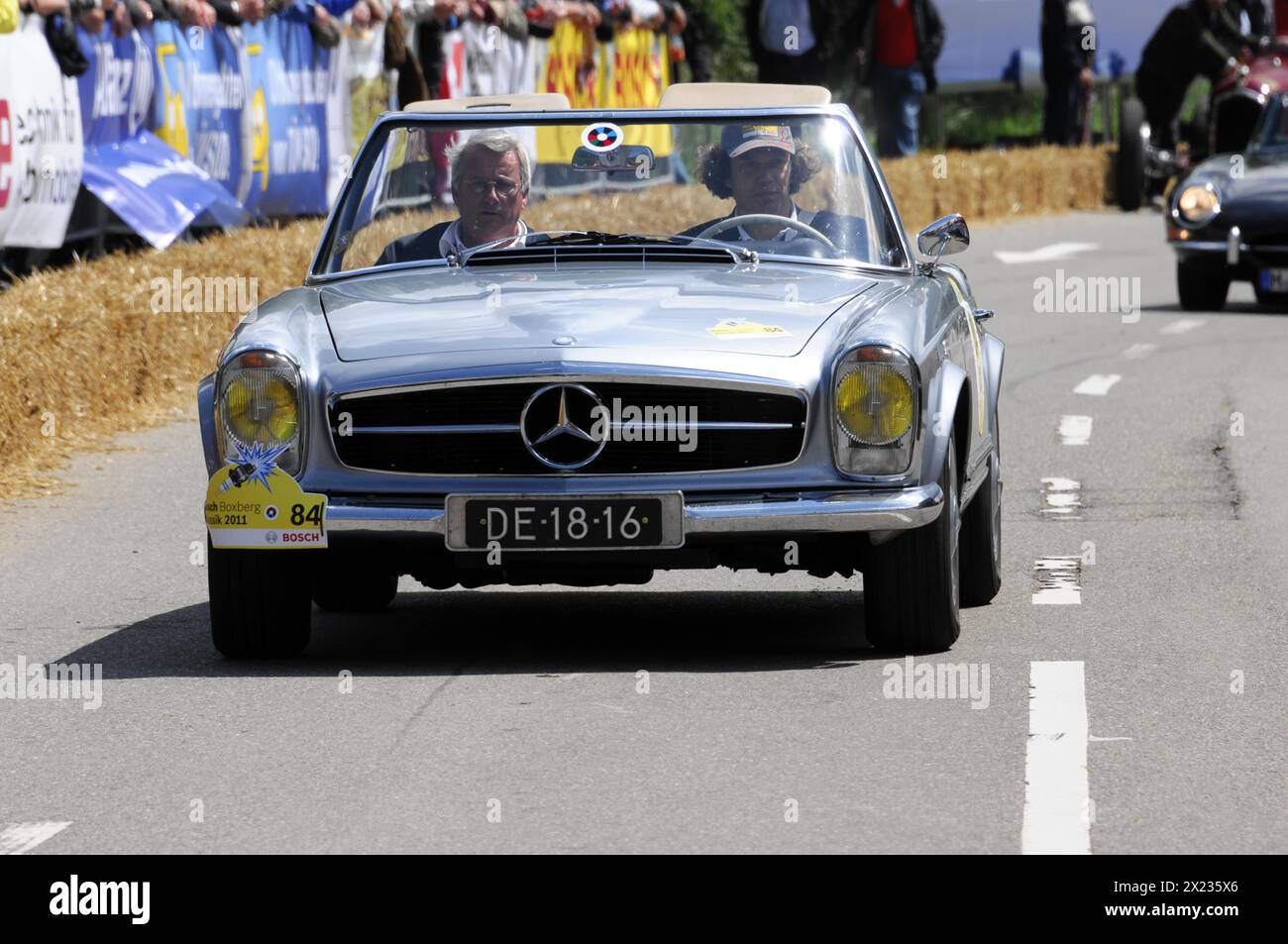A silver Mercedes-Benz 300SL Roadster racing in front of a dense crowd ...