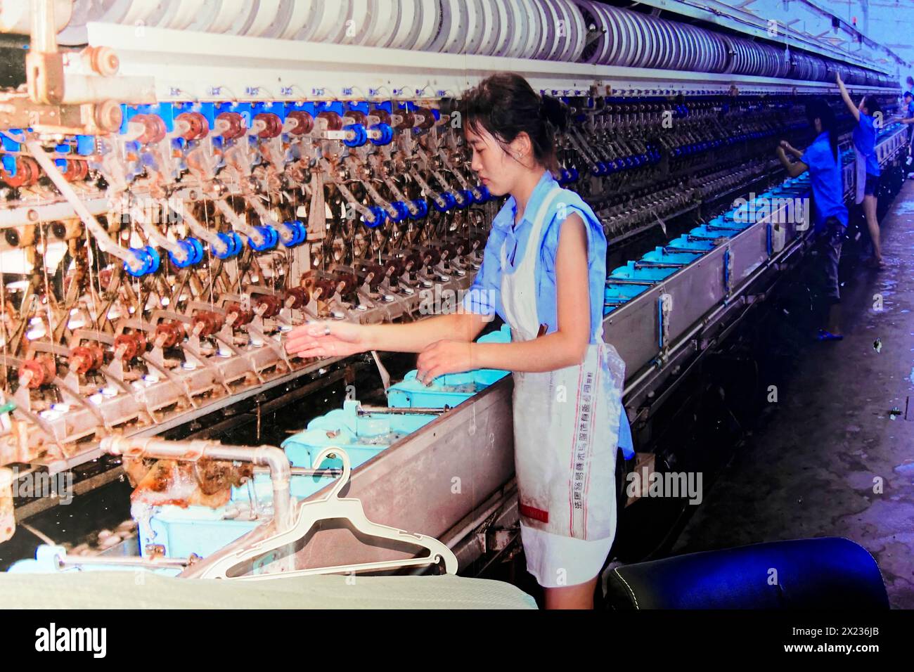 Silk factory Shanghai, A worker operates weaving machines with bobbins ...