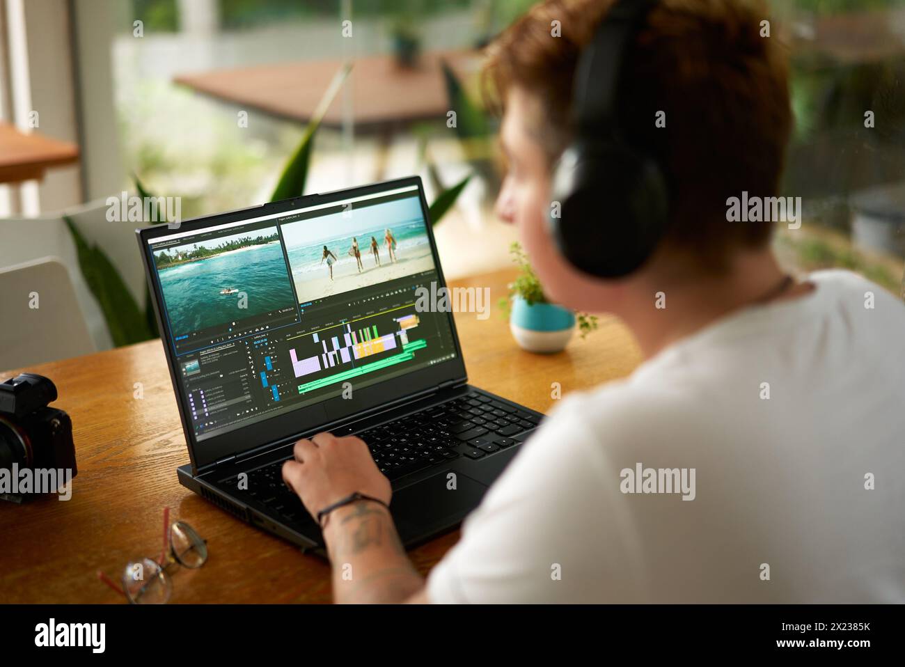 Pro video editor with headphones works on laptop in cafe. Over shoulder ...