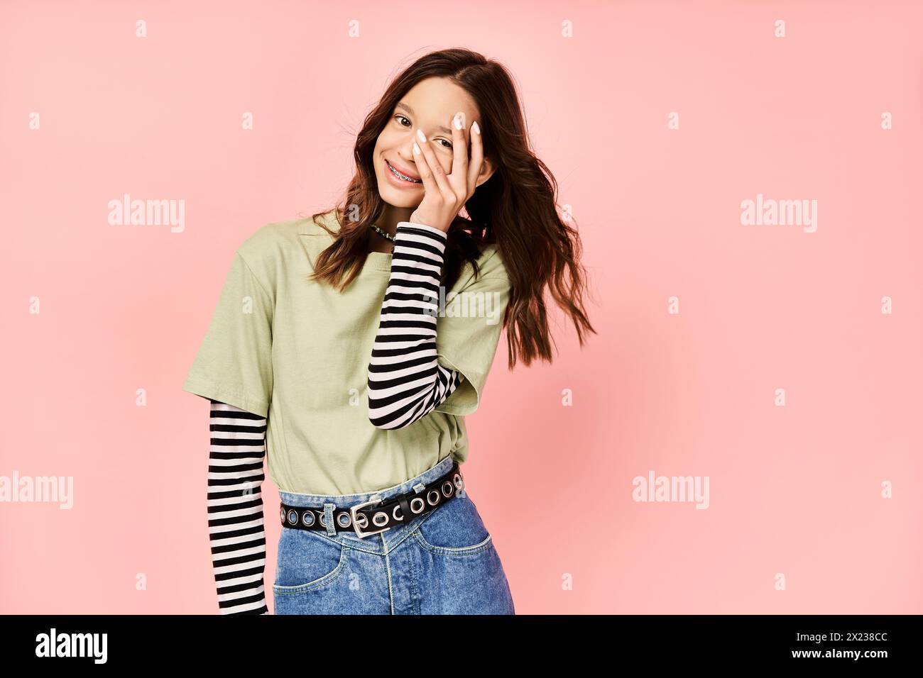 A good looking teenage girl in vibrant attire poses with hands on face ...