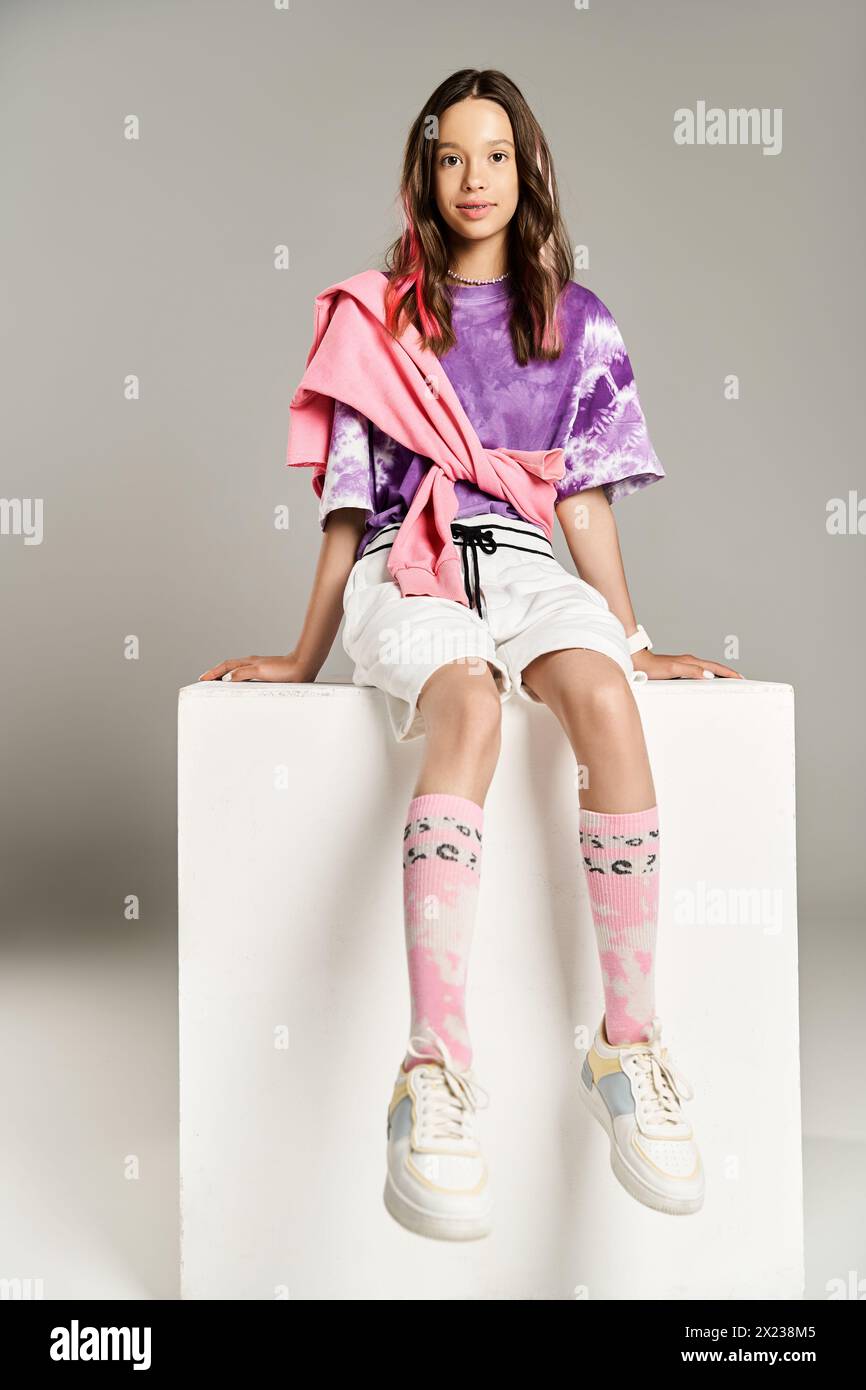 A stylish, vibrant teenage girl confidently sits atop a white block ...