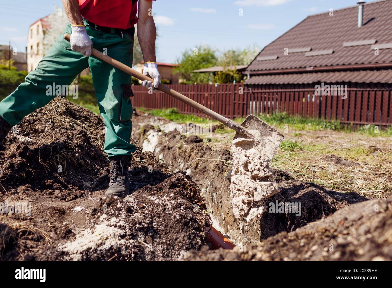 Worker covering pipes in trench with sand using shovel. Building house ...