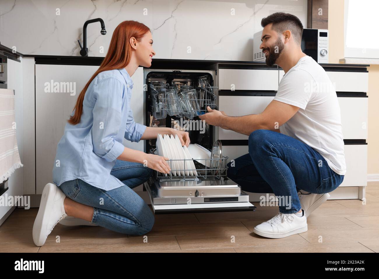 Happy couple loading dishwasher with plates in kitchen Stock Photo - Alamy