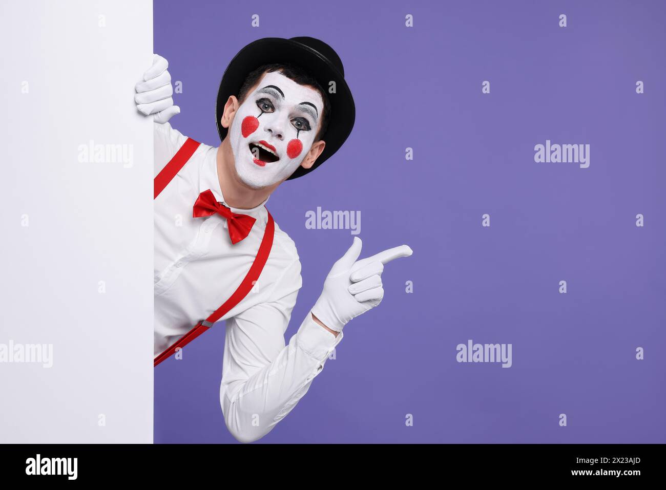 Funny mime artist peeking out of blank poster and pointing at something ...