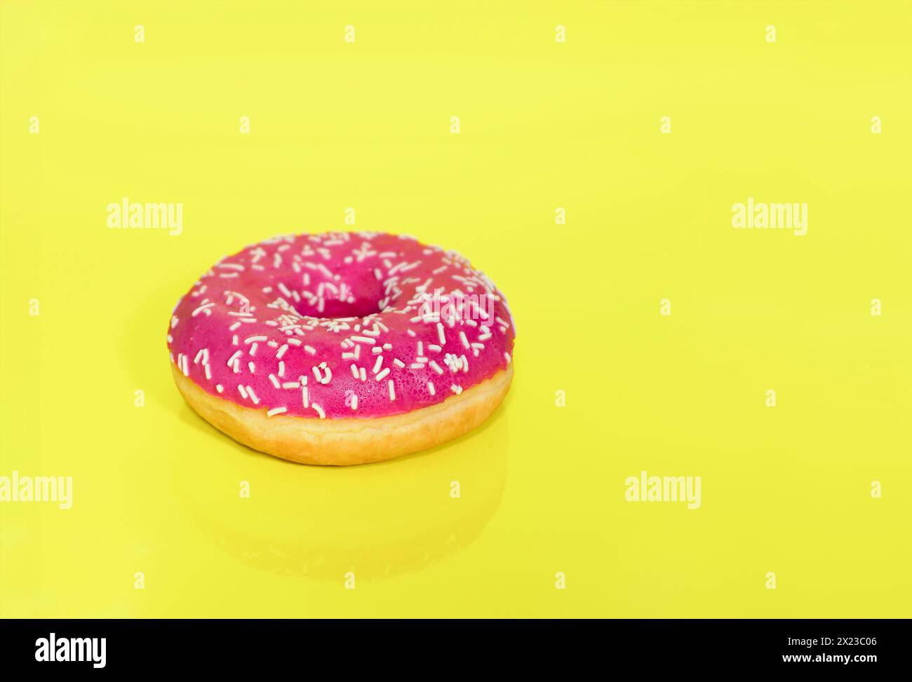 Pink iced Ring Doughnut with sprinkles on, taken on a yellow coloured ...