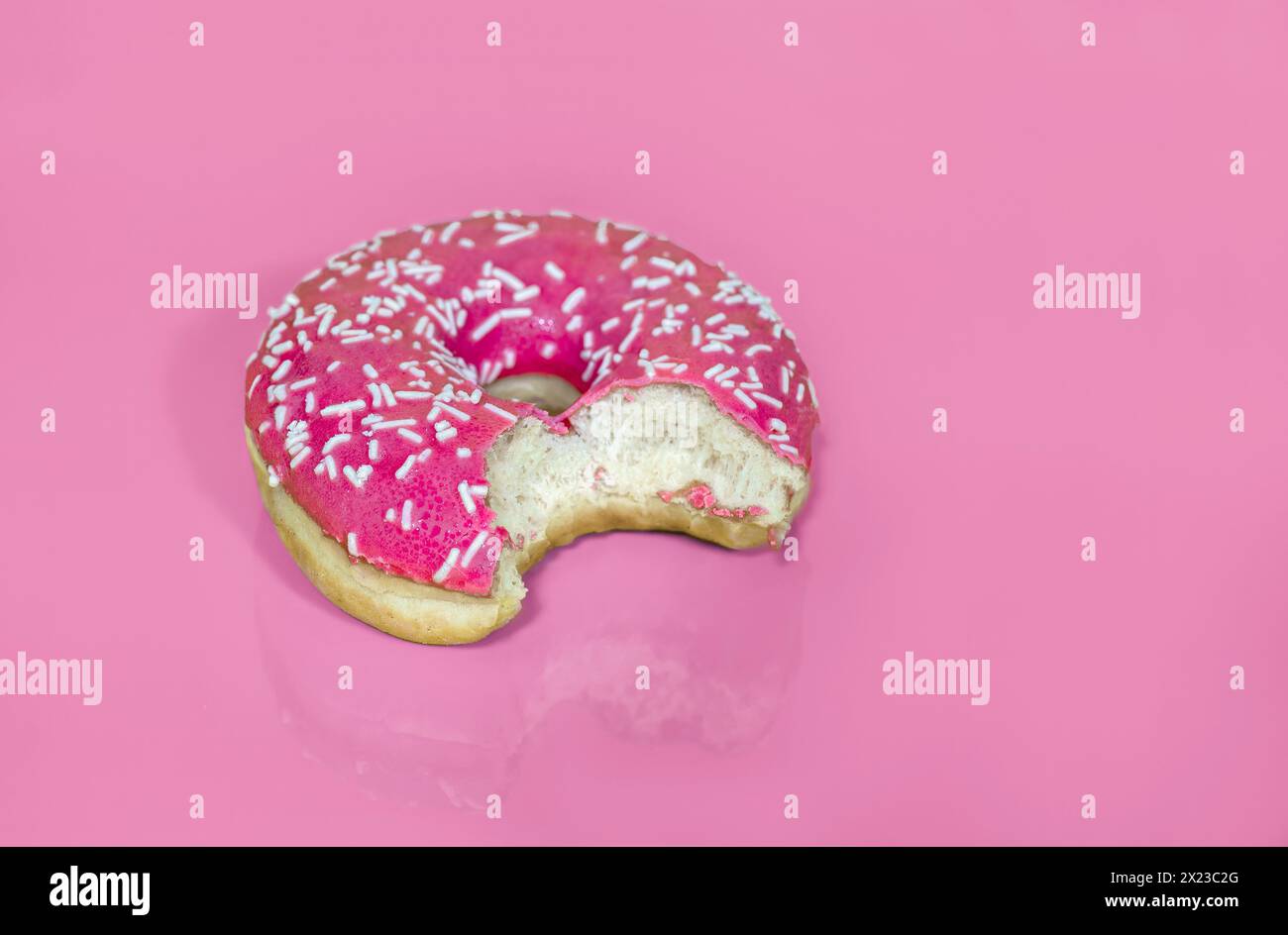 Pink iced Ring Doughnut with sprinkles on with a bite taken out, on a ...