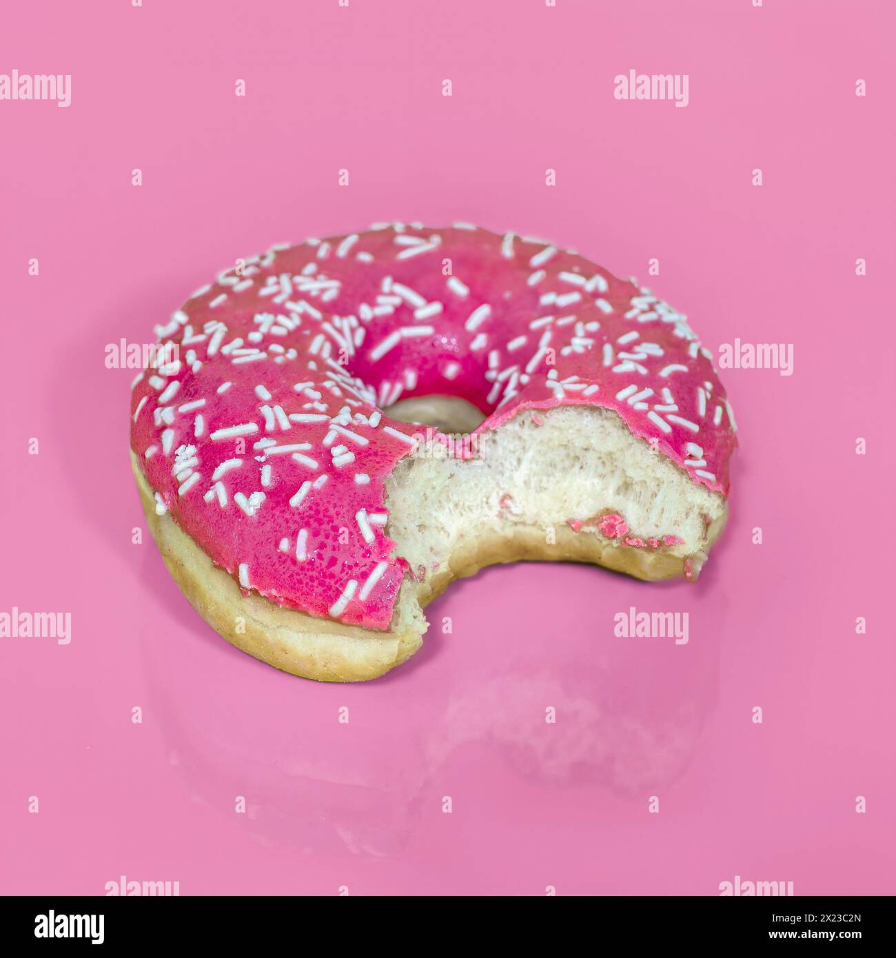 Pink iced Ring Doughnut with sprinkles on with a bite taken out, on a ...