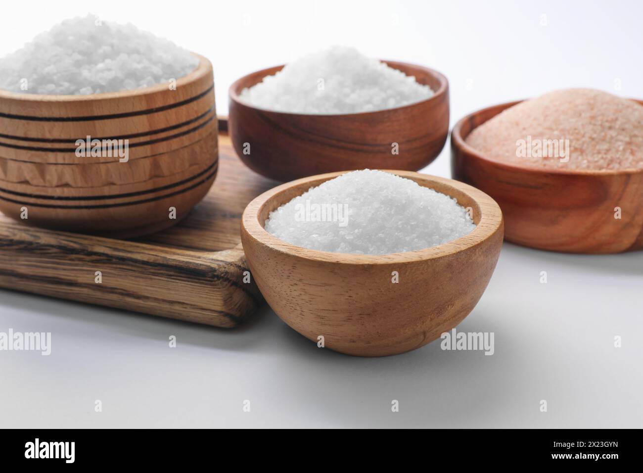 Different types of natural salt in wooden bowls on white background ...