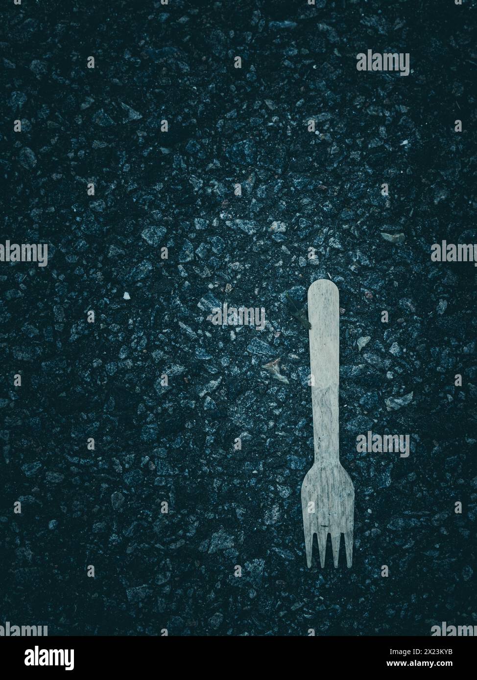 A lone white fork rests atop a dark, textured asphalt surface. The dim ...