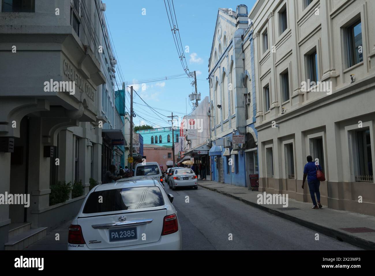 Street with cars and people is lined with old stone houses in Caribbean ...