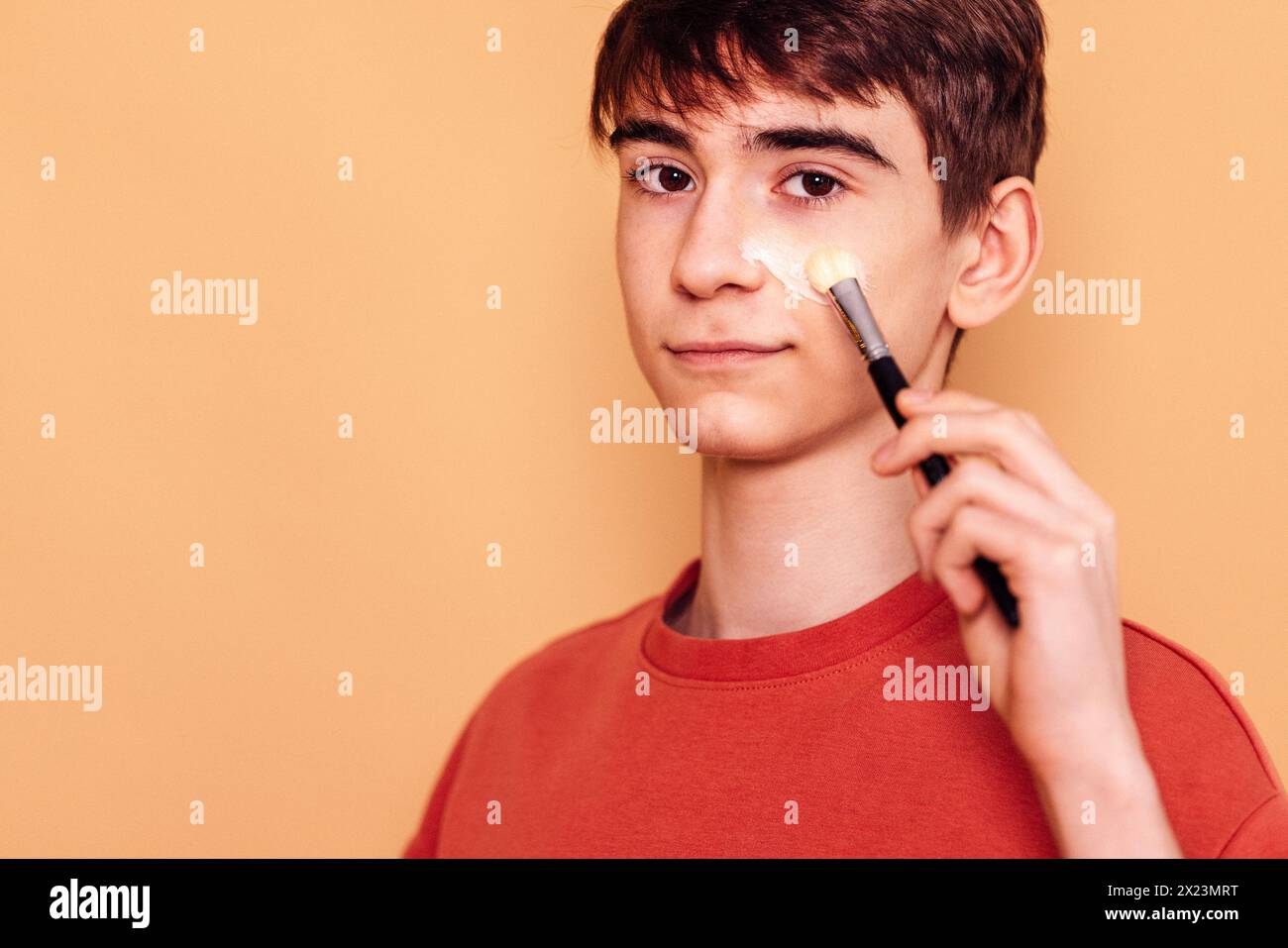 Close-up of a portrait of a male teenager applying cream to his cheek ...