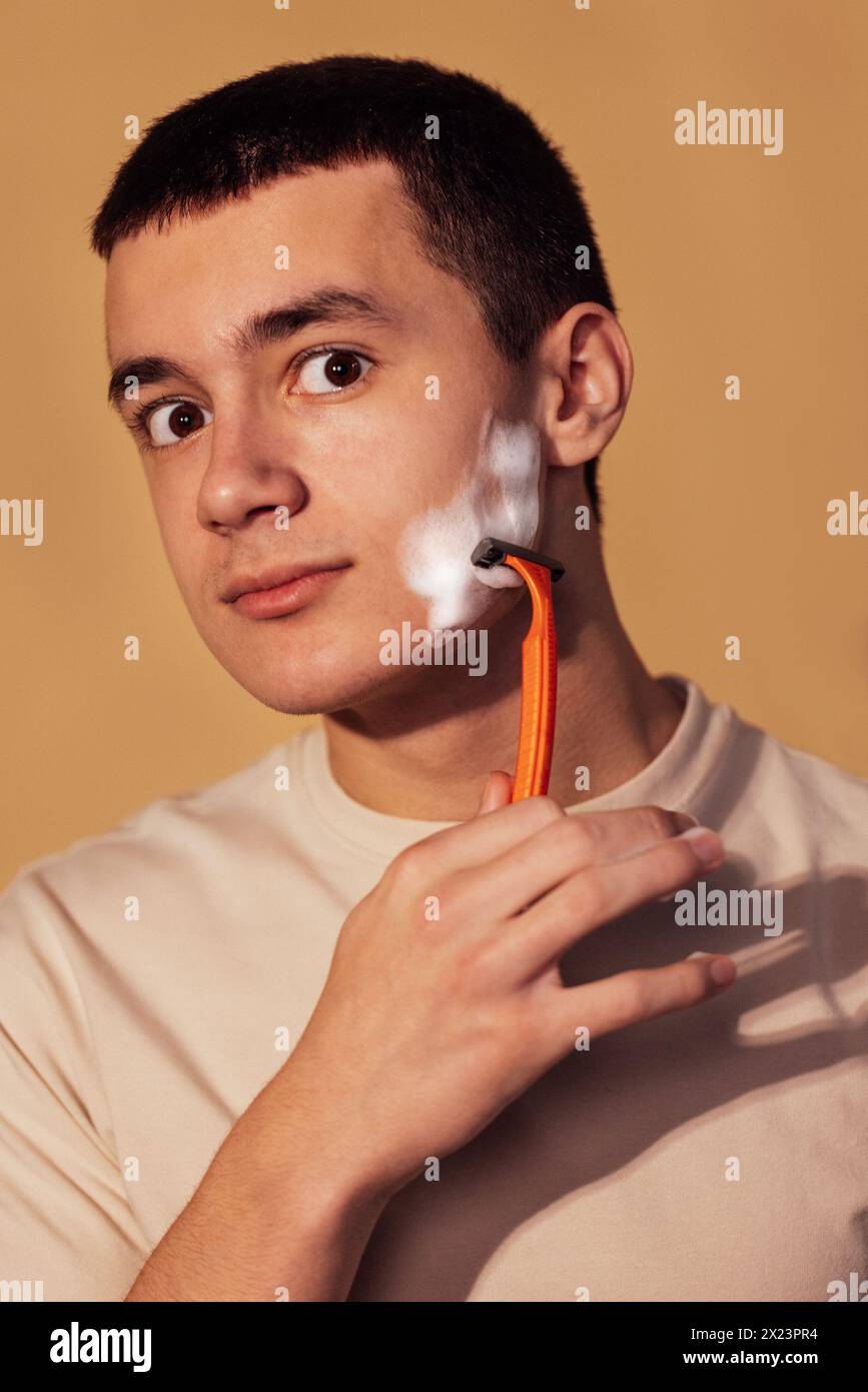 A close-up portrait of a teenager with foam on his cheek and holding a ...