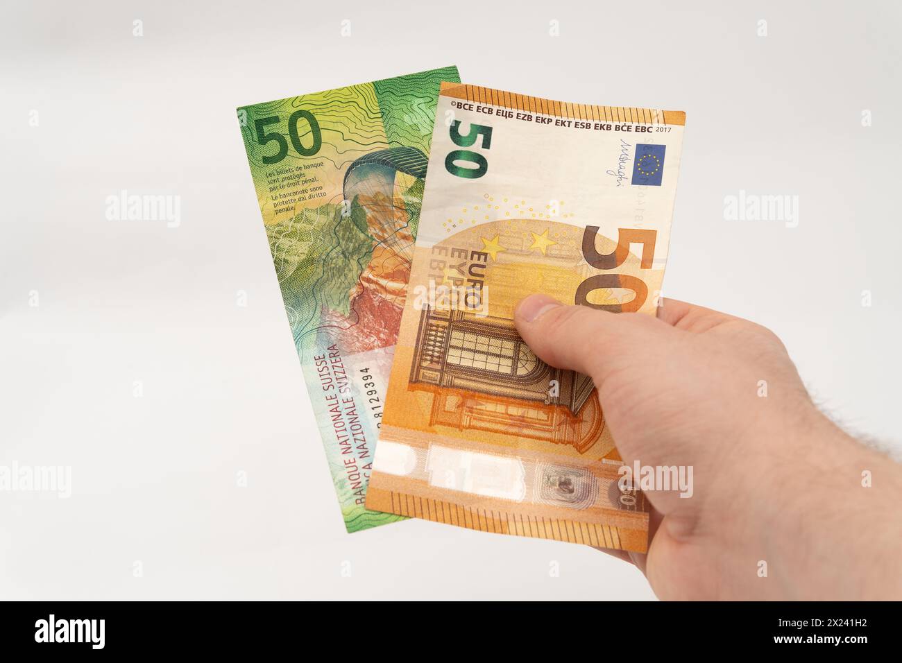 Man holding 50 CHF Swiss franc and 50 EUR Euro banknote paper currency ...