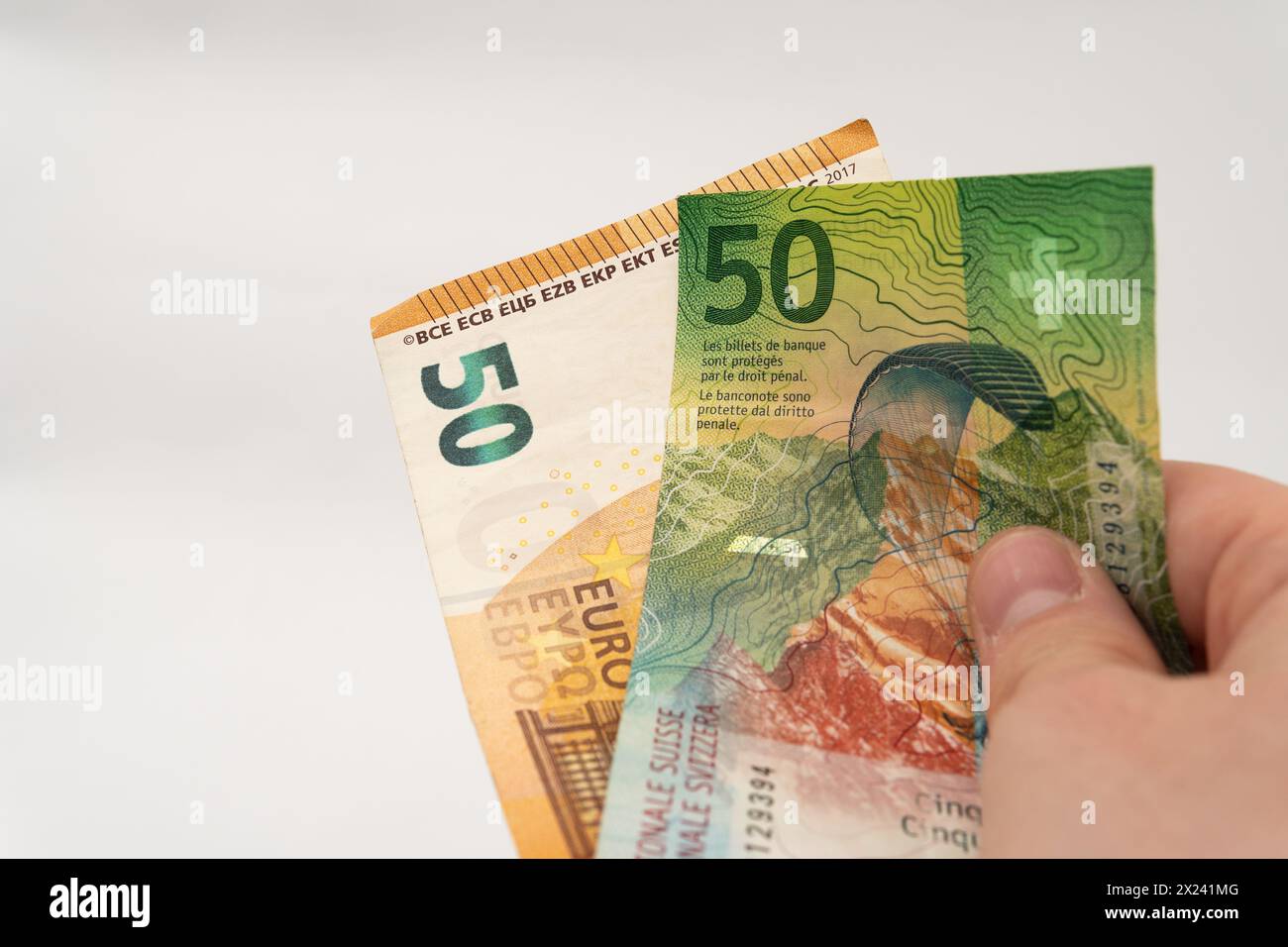 Man holding 50 CHF Swiss franc and 50 EUR Euro banknote paper currency ...