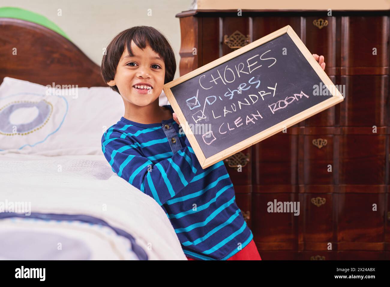 Portrait, chalkboard for chores and boy child in bedroom of home with ...