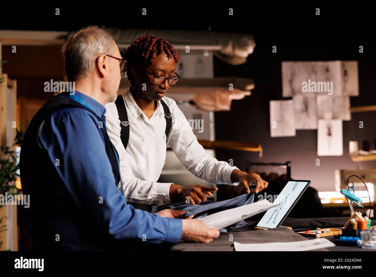 Master couturier and apprentice looking at handdrawn sketches to determine necessary adjustments ...