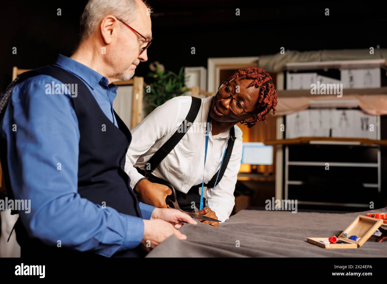 Helpful old master suitmaker and happy tailor apprentice cutting fabric ...