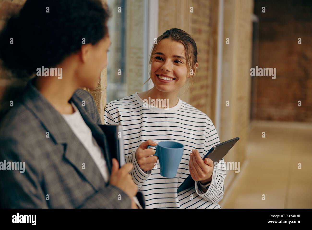 Smiling women colleagues speak laughing enjoy leisure time at workplace ...