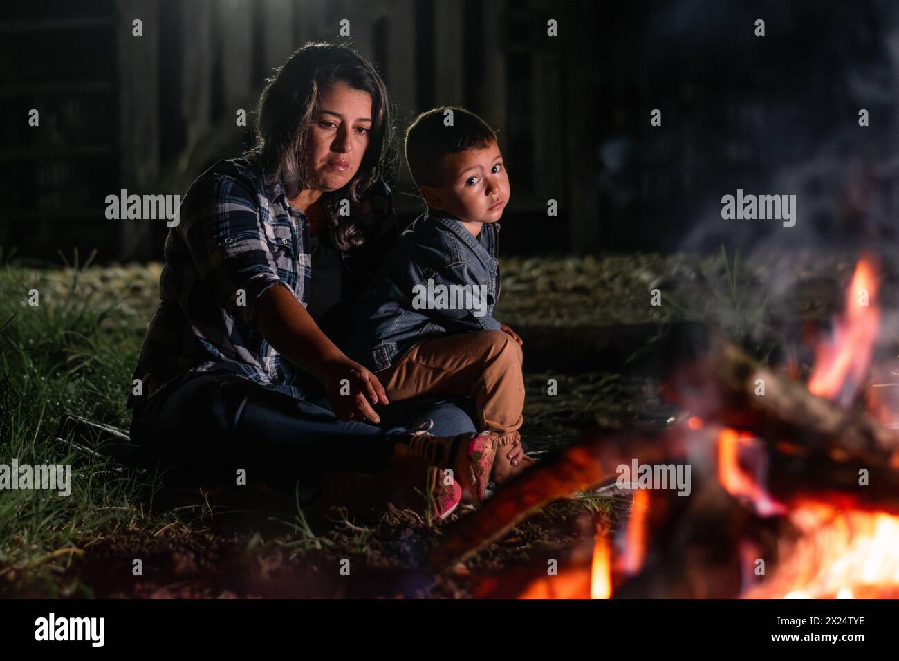 young latin woman carrying her son, sitting in front of a campfire at ...