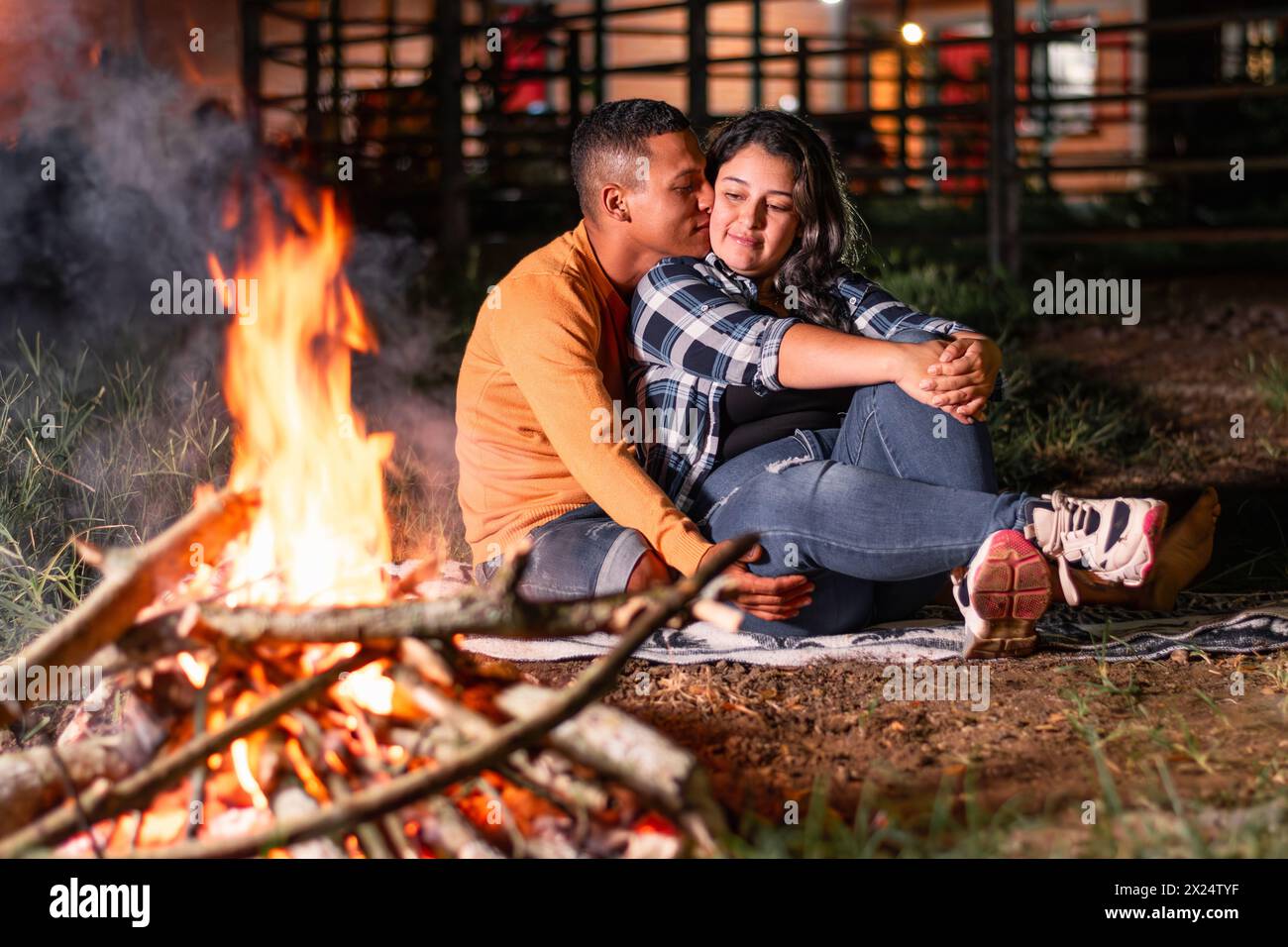 young Latin peasant couple, sitting by a campfire at night, embracing ...