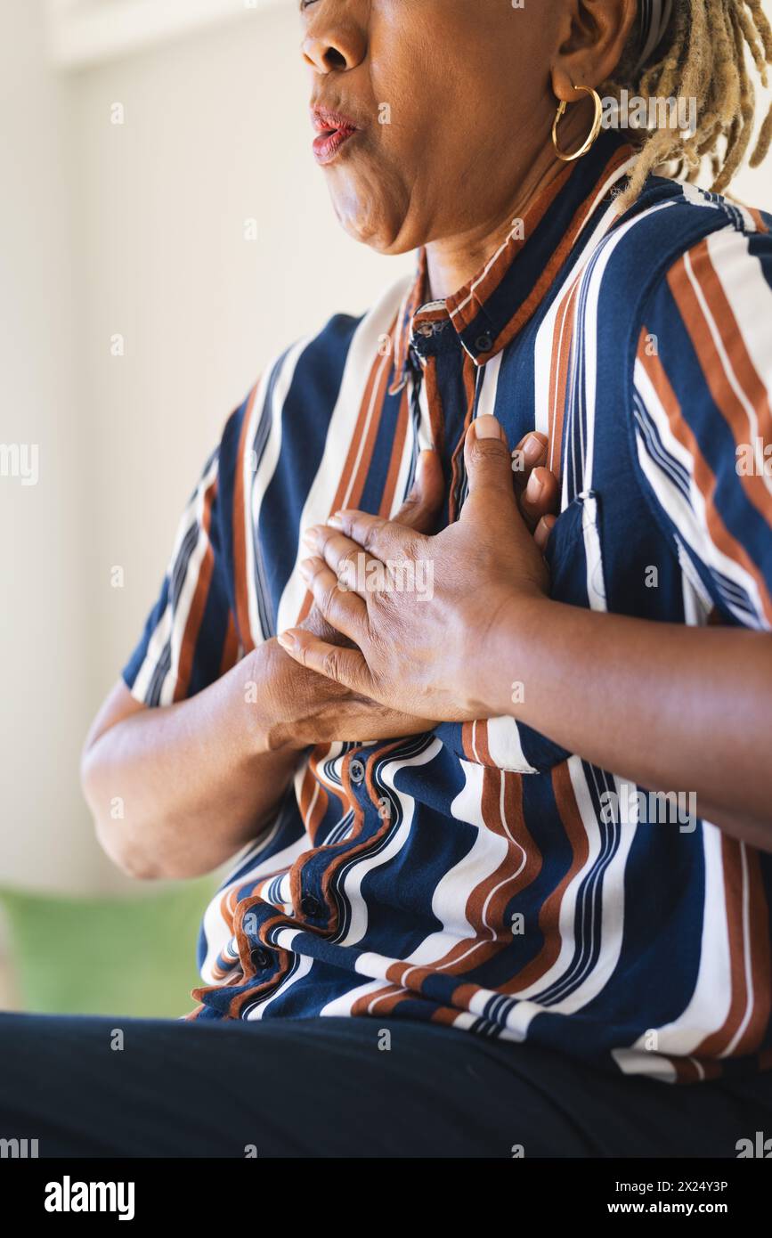 A senior African American woman with gold earrings is holding her chest ...