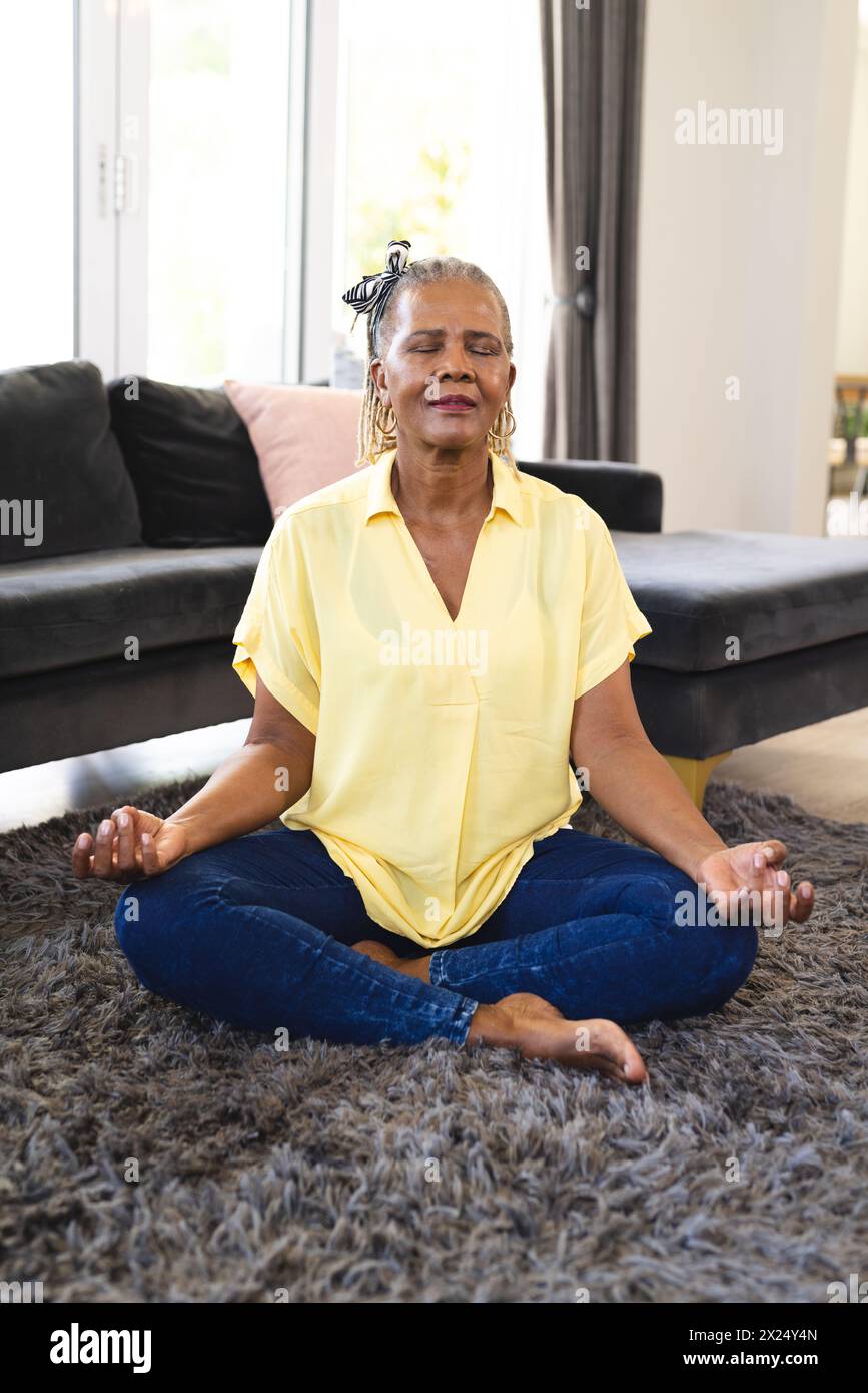 African American senior woman sitting cross-legged on rug at home ...