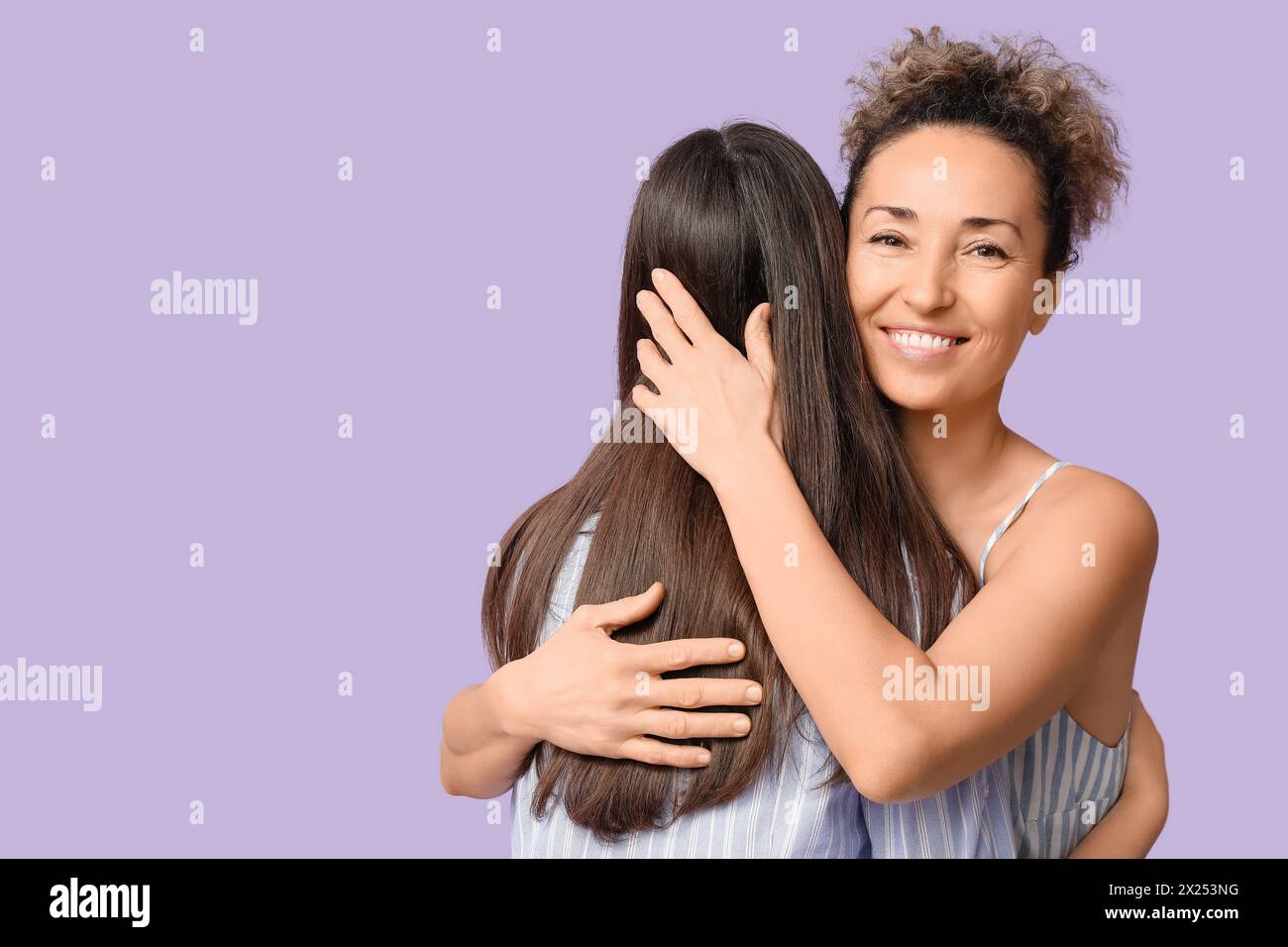 Beautiful mature woman hugging her teenage daughter on lilac background. Mother's day Stock ...
