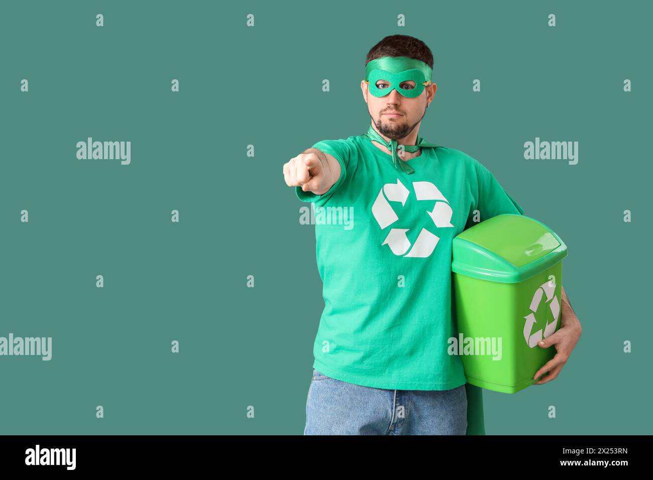 Young man dressed as eco superhero with garbage bin pointing at viewer ...