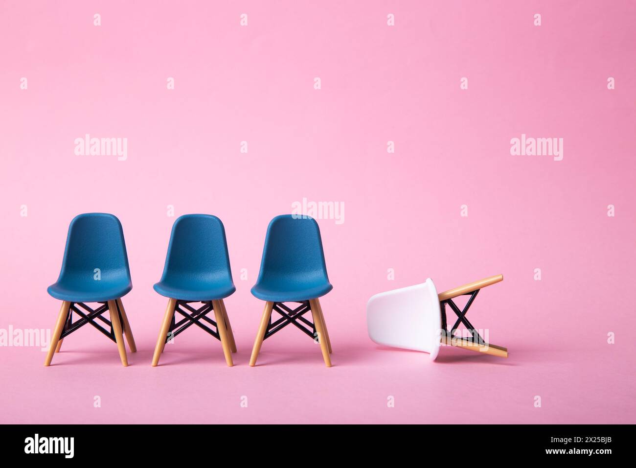 Row of blue chairs and a white one falling down Stock Photo - Alamy