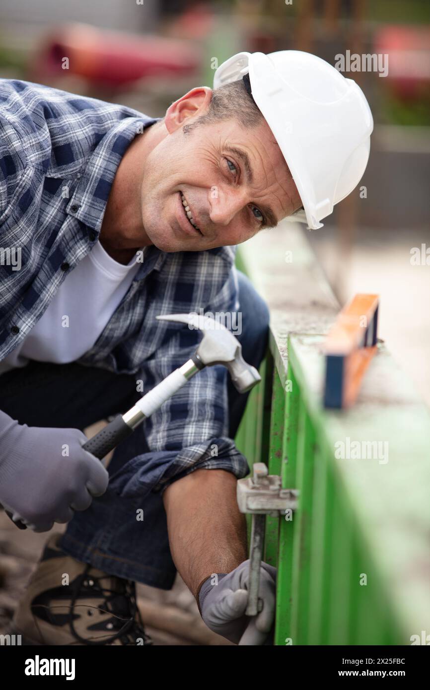 good looking handyman at building site hammering Stock Photo - Alamy