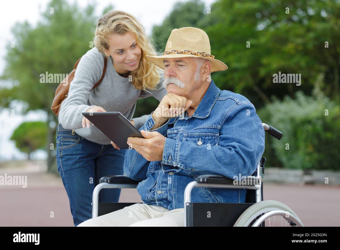 woman showing tablet screen to disabled elderly man Stock Photo - Alamy