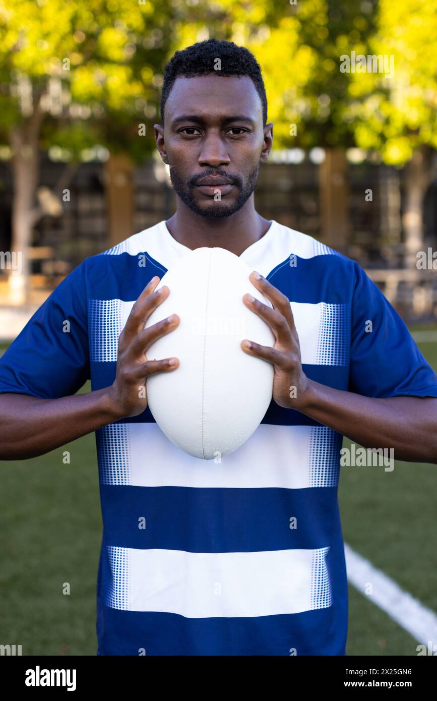 African American young male athlete holding a rugby ball on field ...