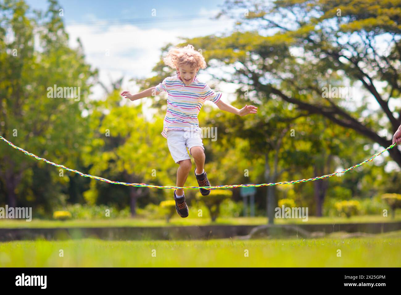 Happy kids play outdoor. Children skipping rope in sunny garden. Summer ...